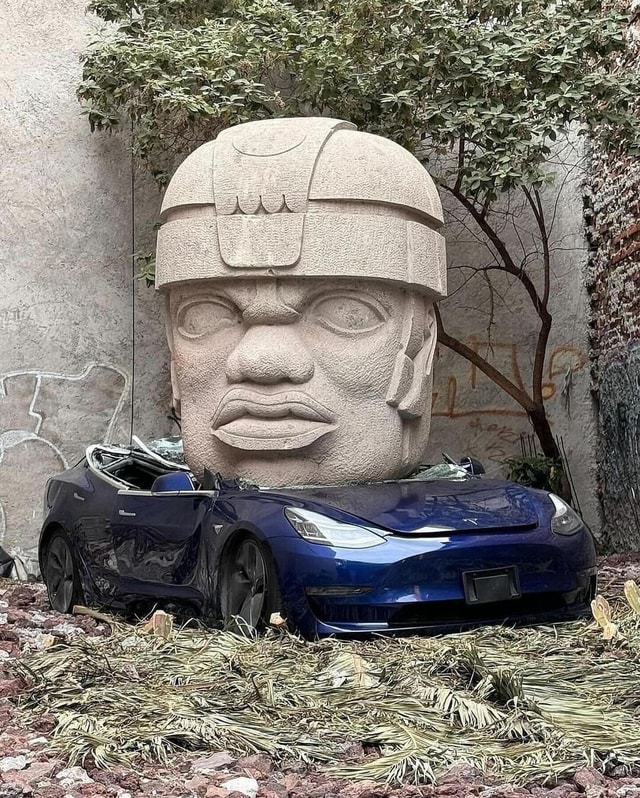 A tesla model 3 being crushed by an olmec head. it symbolizes the ...